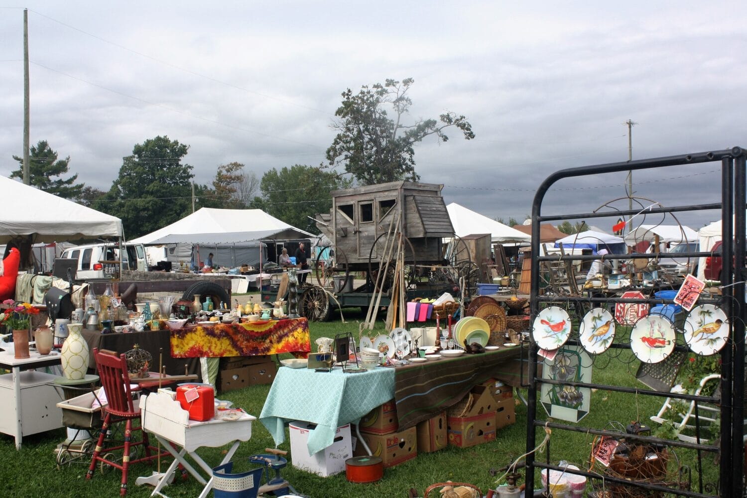 the outdoor flea market scene with a variety of vintage items on display under a cloudy sky