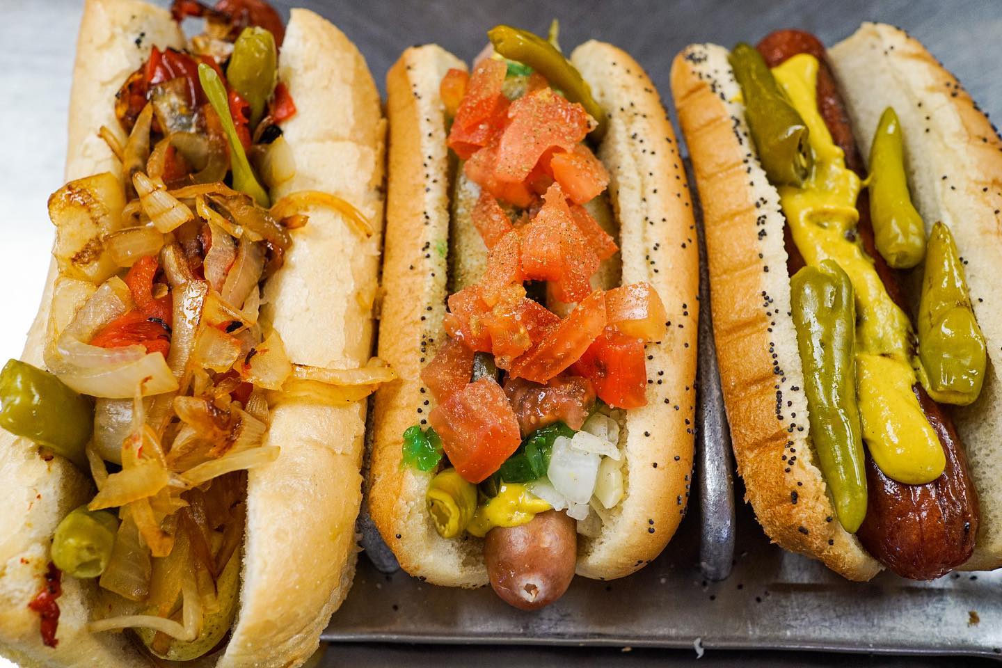 three varieties of hot dogs with generous toppings on a metal tray