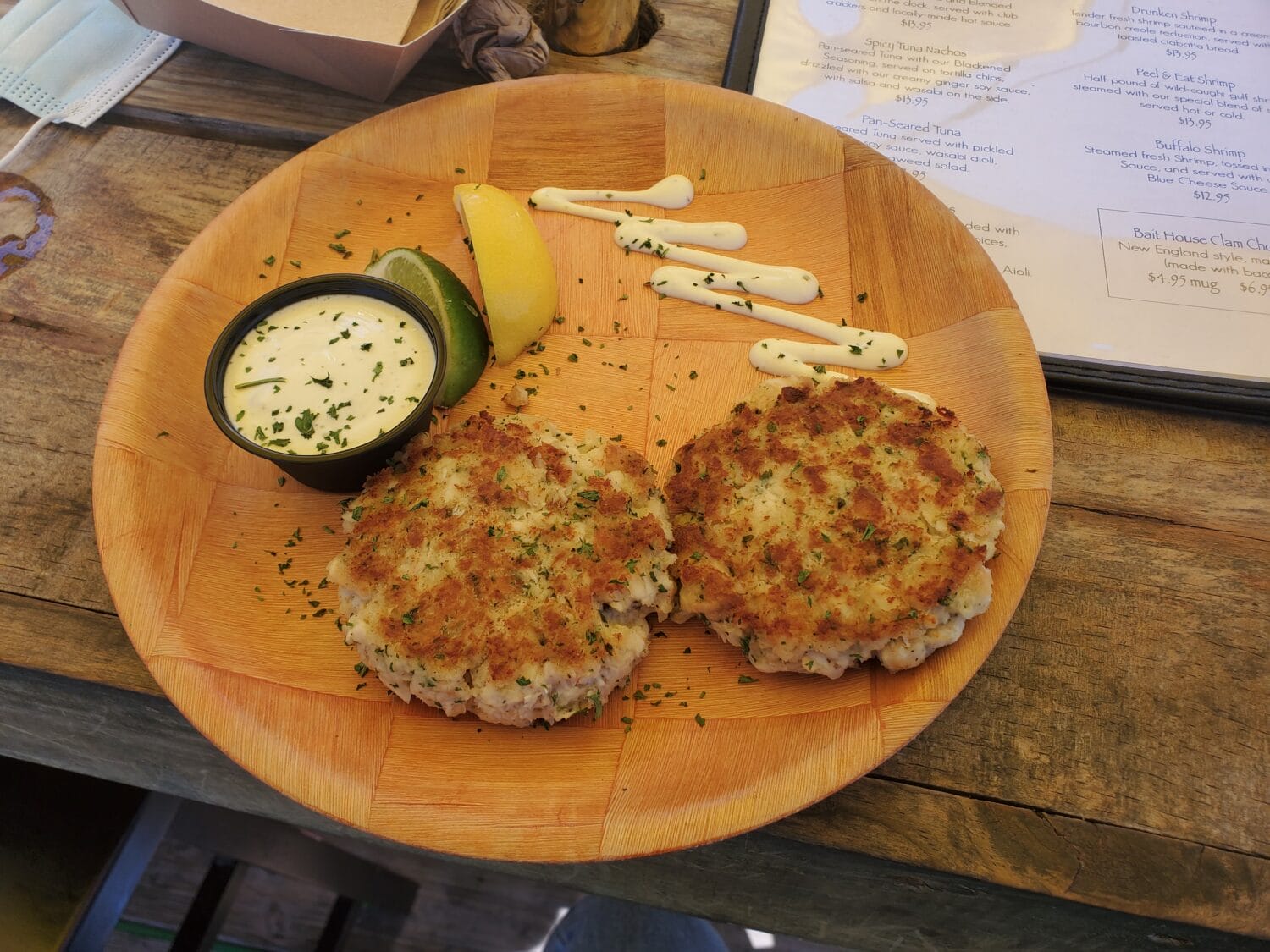 two crab cakes served with a side of tartar sauce and a lemon wedge on a wooden serving board