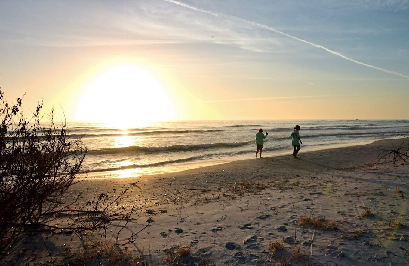 two people running on a beach at sunset with the sun low on the horizon