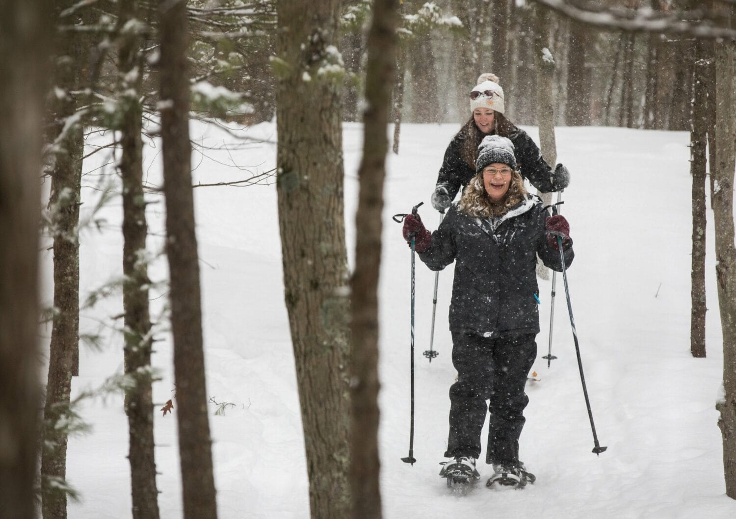 two people snowshoeing through a dense pine forest in muskegon luge adventure sports park