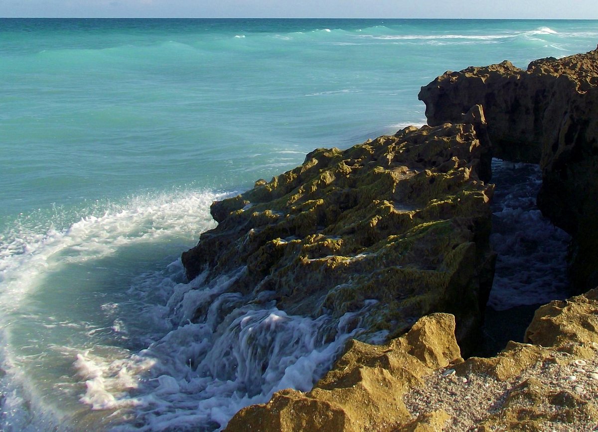 waves crashing against rocky limestone formations on a sunny beach