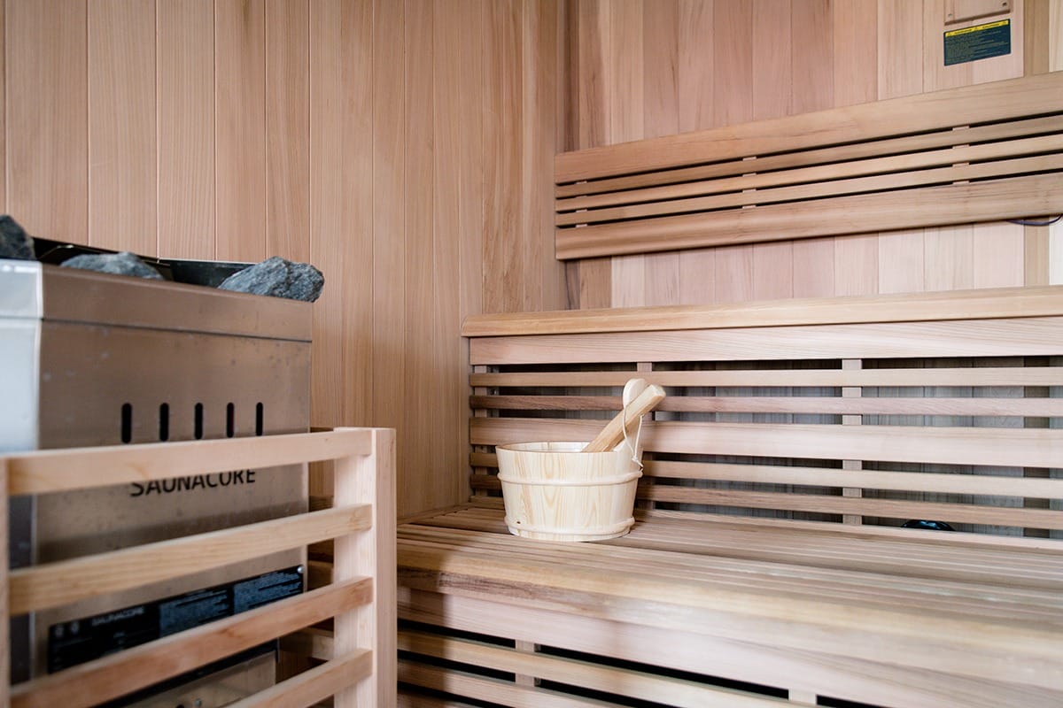 wooden sauna room interior with a heater filled with rocks and a wooden bucket with a ladle