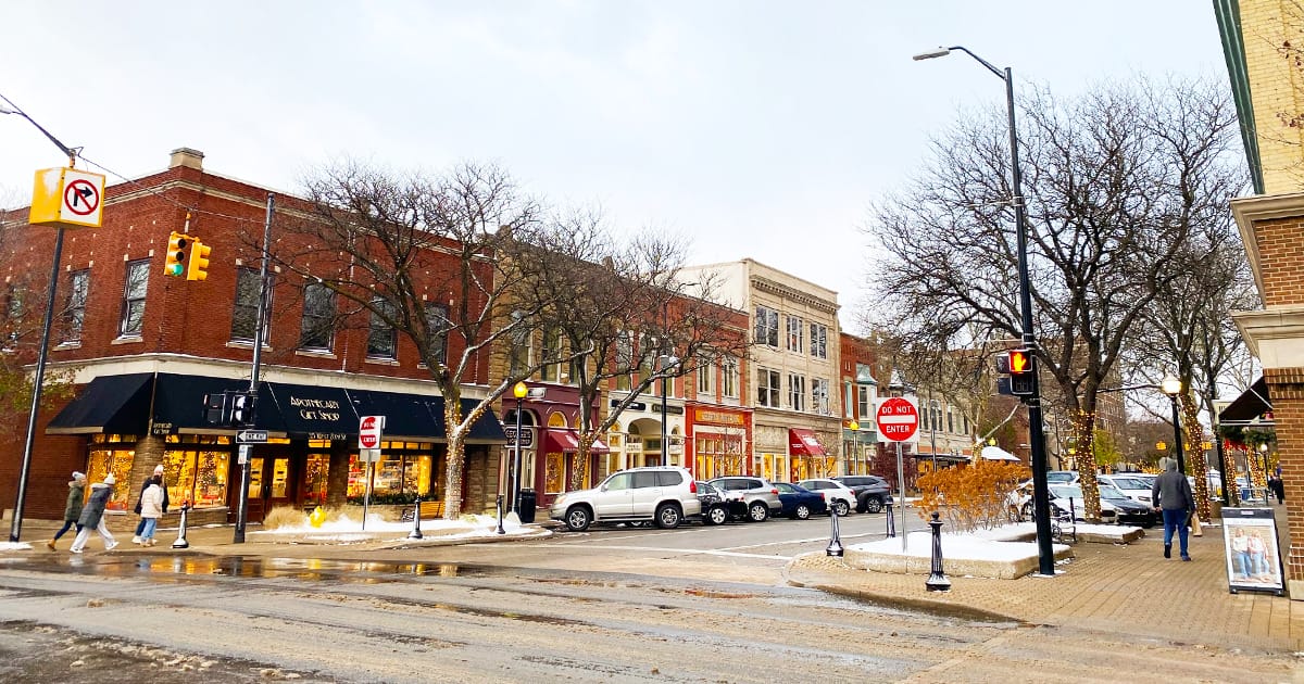 a bustling corner of the snowy downtown area of holland, lined with quaint shops and historic buildings, with pedestrians walking and cars parked along the curbside