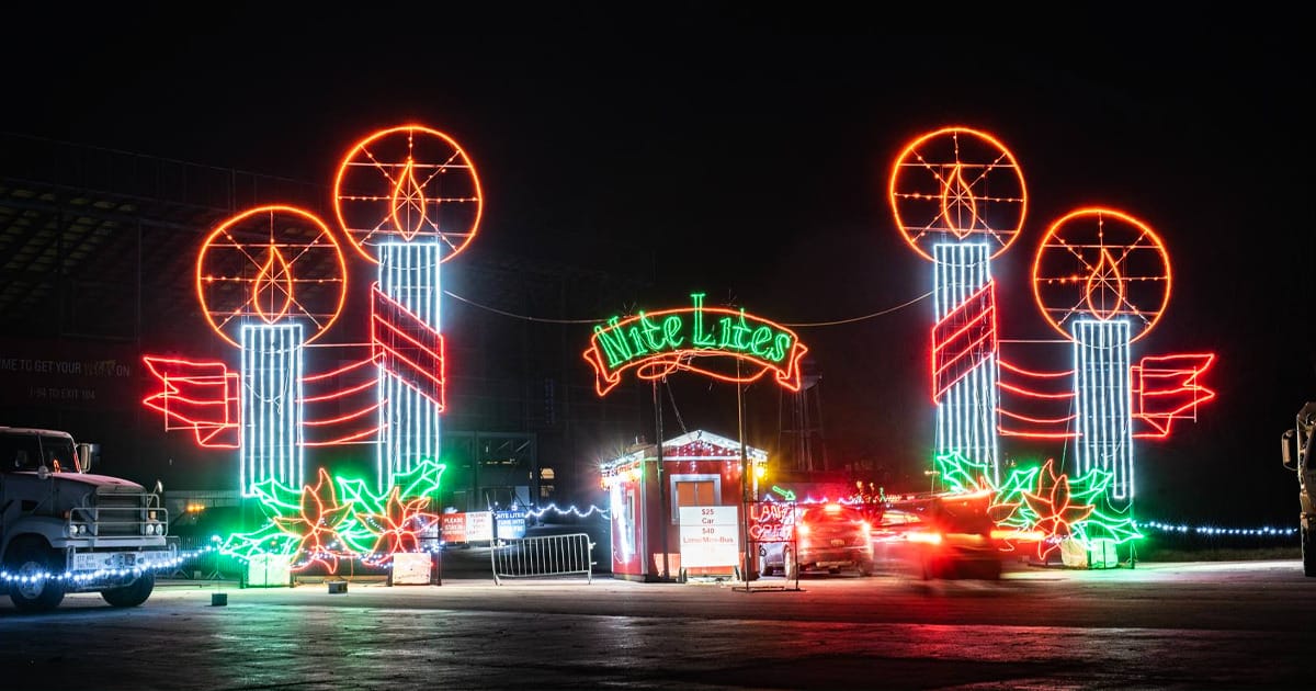 a vibrant nighttime scene at michigan international speedway during the nite lites holiday display with glowing neon outlines of windmills and flowers, and blur of passing cars