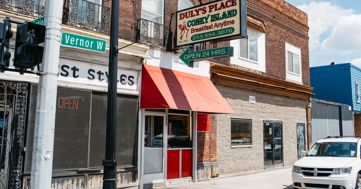 the exterior of duly's place, boasting a vintage sign that reads breakfast anytime and highlighting its 24 hour service on a sunny street corner