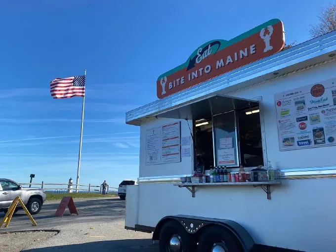 A classic white food truck against a brilliant blue Maine sky, with Old Glory waving proudly – this is where lobster roll dreams come true. Photo credit: Aaron Bennett