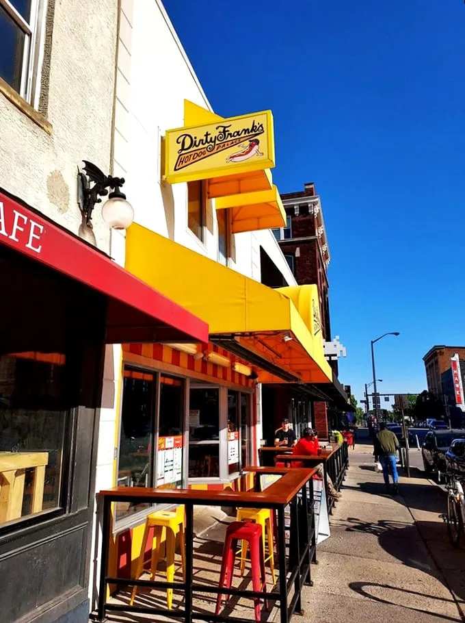 Yellow beacon of hope! Dirty Frank's exterior promises a hot dog adventure with its vibrant awning and inviting patio. Comfort food paradise awaits.