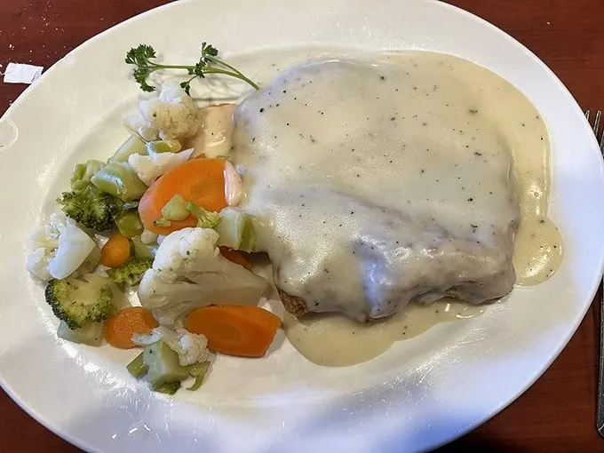 Steam rises from perfectly seasoned country fried steak, swimming in creamy gravy alongside fresh, crisp vegetables.