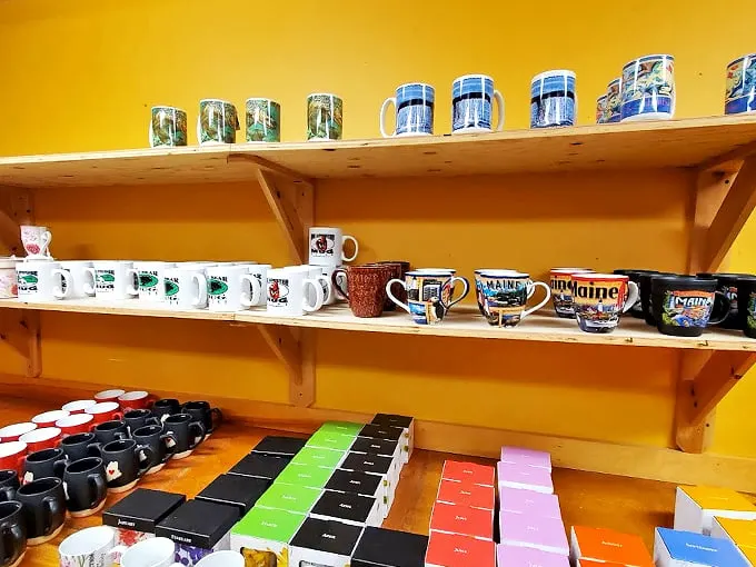 A rainbow of Maine mugs tells stories of lighthouses and lobsters, perfect for sipping morning coffee with a side of nostalgia.