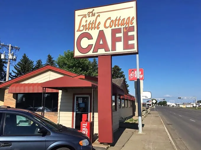 Welcome to flavor town! The Little Cottage Café's sign promises big taste in a small package, like a culinary TARDIS waiting to be explored.