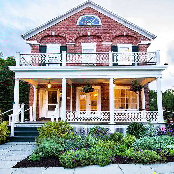 A storybook come to life! This charming red brick façade with its white-columned porch whispers tales of lazy summer evenings and hot cocoa by the fire.