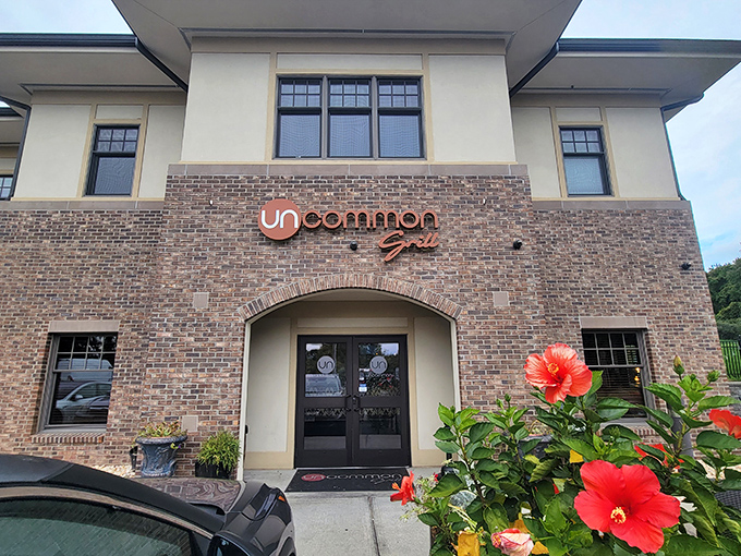 The stately brick facade of Uncommon Grill welcomes you with vibrant hibiscus flowers, promising an experience that's anything but ordinary