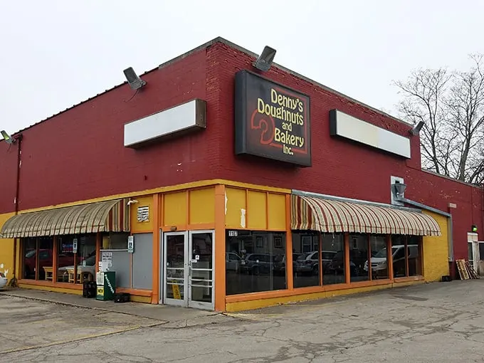 Welcome to carb heaven! Denny's Doughnuts and Bakery stands like a beacon of sugary hope on the corner, its red brick and yellow awnings promising sweet salvation.