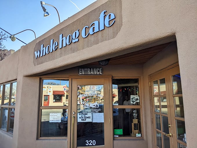 Welcome to flavor town! Whole Hog Café's adobe exterior is like a siren song for barbecue lovers, with that American flag waving you in for a taste of smoky paradise.