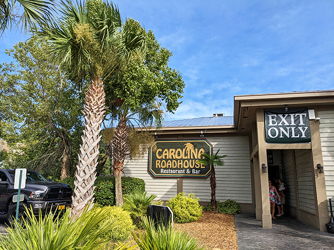 Palm trees stand sentinel alongside the unassuming exterior of Carolina Roadhouse, where culinary treasures await behind that modest "EXIT ONLY" sign.