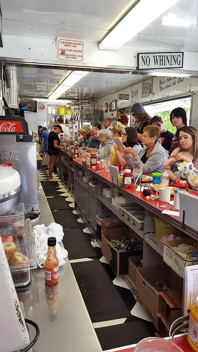 At full capacity, this is democracy in action—fifteen strangers united by eggs and coffee, with a strict "NO WHINING" policy enforced from above.
