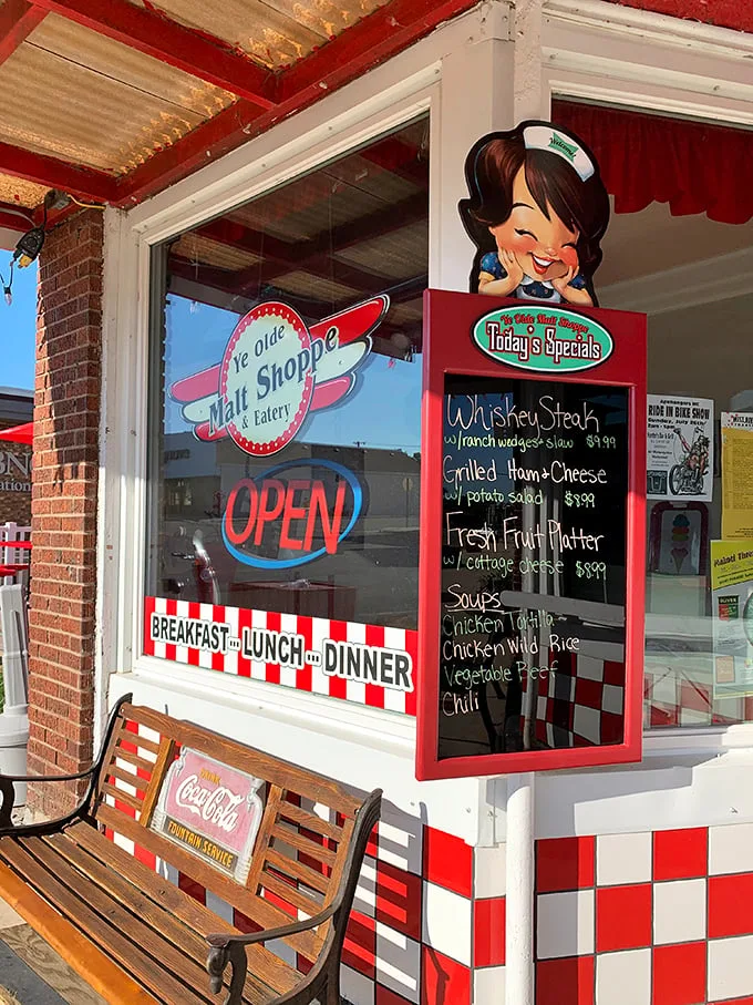 The store window: where promises of deliciousness meet small-town charm. That cartoon waitress knows something we don't – probably where they hide the extra sprinkles.