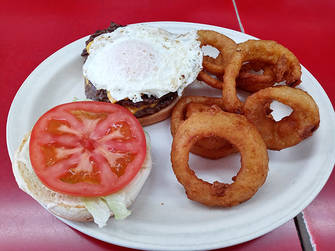 The burger arrives with onion rings that look like edible Olympic symbols. That egg on top isn't just food—it's the championship belt of breakfast add-ons.