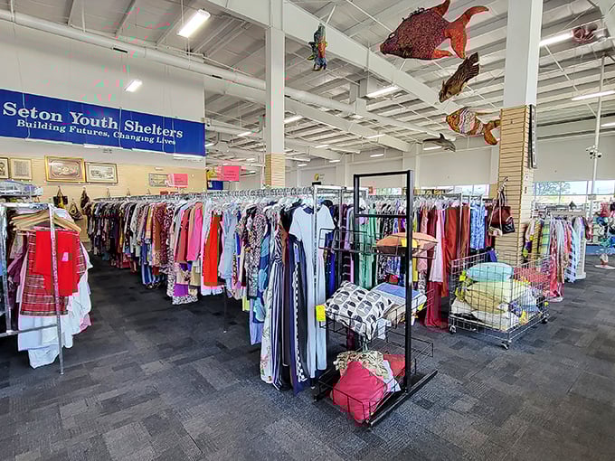 Beneath colorful fish sculptures swimming overhead, racks of potential wardrobe transformations await. The Seton Youth Shelters banner reminds shoppers their purchases support a worthy cause.