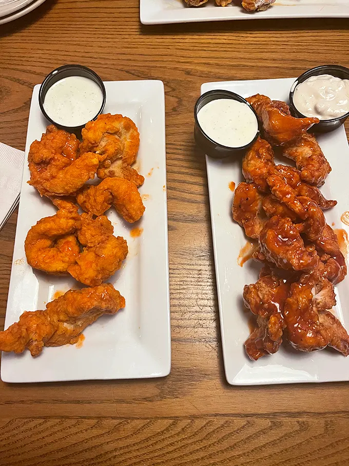 Two plates of wing perfection—one crispy, one saucy—flanked by house-made dipping sauces. This is what dreams look like at 2 a.m.
