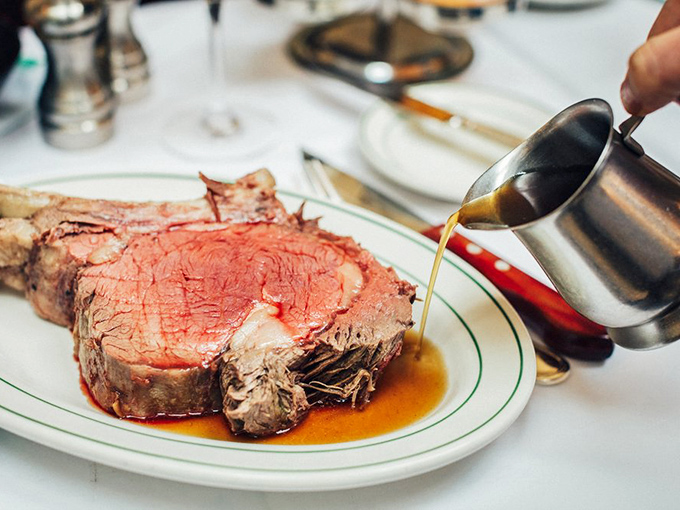 The prime rib arrives like royalty with its own entourage—a golden pool of jus that should be classified as a controlled substance.