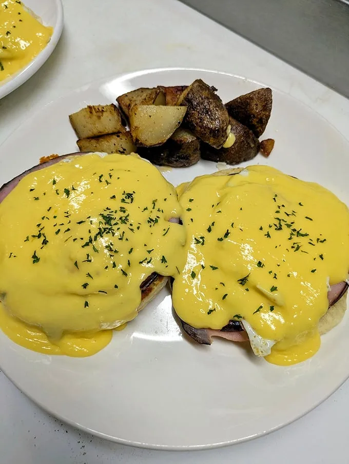 Eggs Benedict with hollandaise so golden it deserves its own Fort Knox, served with home fries that achieve that mythical crispy-outside, tender-inside perfection.