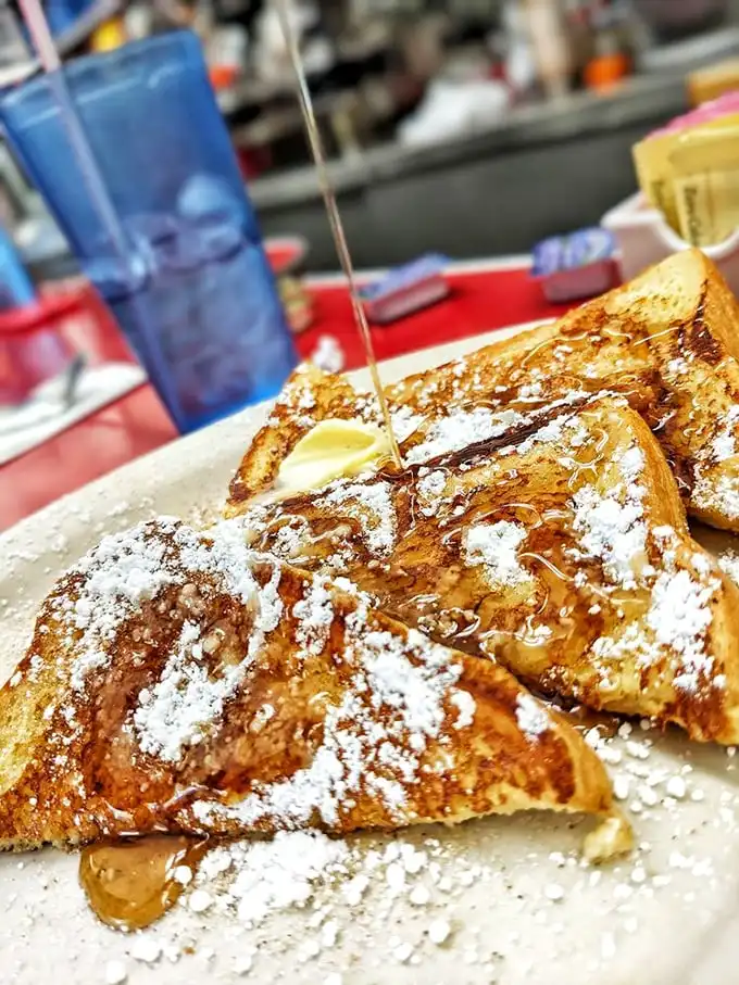 French toast that belongs in the Louvre—golden, dusted with powdered sugar, and a stream of maple syrup cascading down like a breakfast waterfall.