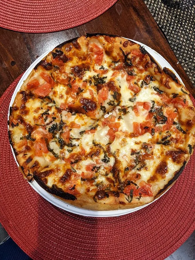 Margherita magic! Fresh tomatoes and basil play hide-and-seek with melted mozzarella, creating a pizza that's basically a portable Italian vacation.