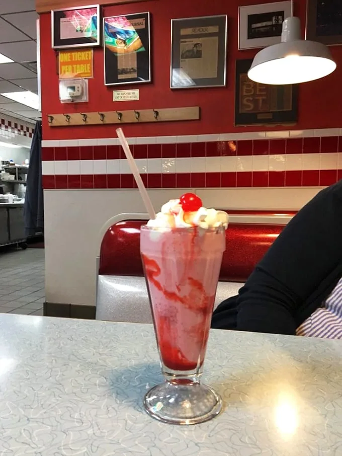 The strawberry shake arrives like a 1950s dream, complete with whipped cream crown and cherry tiara—dessert masquerading as a legitimate beverage.