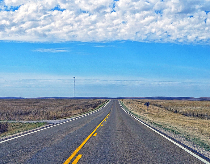 The road stretches toward infinity, where Kansas sky meets prairie in a perfect horizon. This is freedom defined.