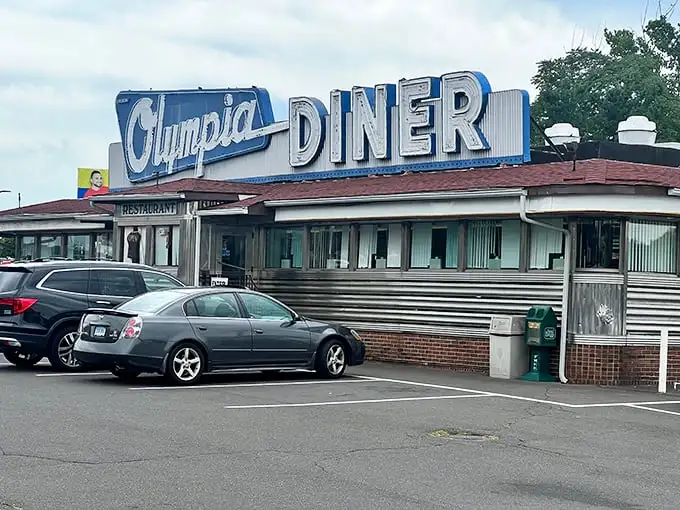 That neon sign isn't just advertising—it's a time machine. The Olympia's iconic blue and pink glow has been guiding hungry travelers home since Eisenhower was president.