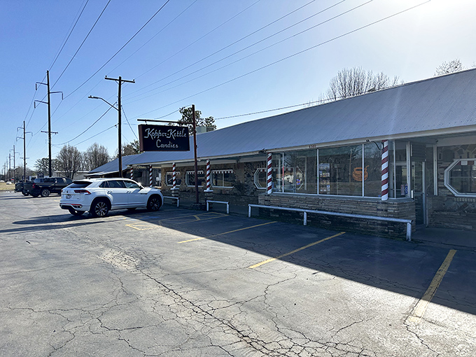 The iconic storefront of Kopper Kettle Candies stands resilient against Arkansas rain, its candy-striped poles promising sweet refuge from ordinary life.