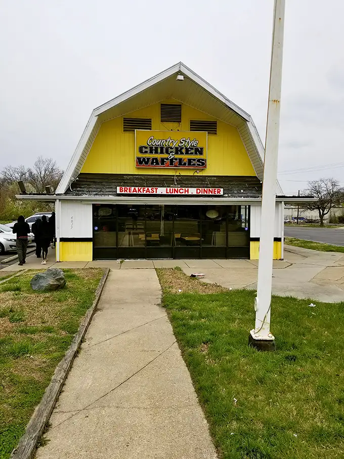 The distinctive peaked roof and cartoon sign of Country Style Chicken And Waffles beckons hungry travelers like a lighthouse for comfort food enthusiasts.