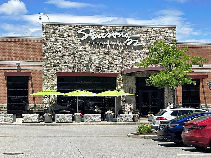 The stone facade of Seasons 52 stands like a culinary lighthouse, beckoning hungry travelers with its warm glow and those unmistakable bright green umbrellas.
