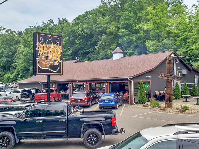 The rustic cabin exterior of Bear's Den Steakhouse promises a wilderness experience with gourmet credentials. That wooden bear statue isn't just decoration—it's a preview of coming attractions.