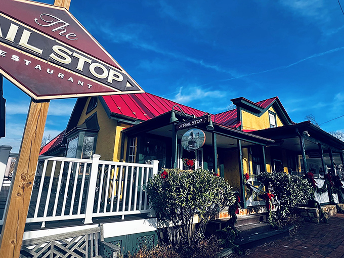 The charming yellow exterior of The Rail Stop beckons like an old friend, promising comfort and culinary delights beside that distinctive red sign.