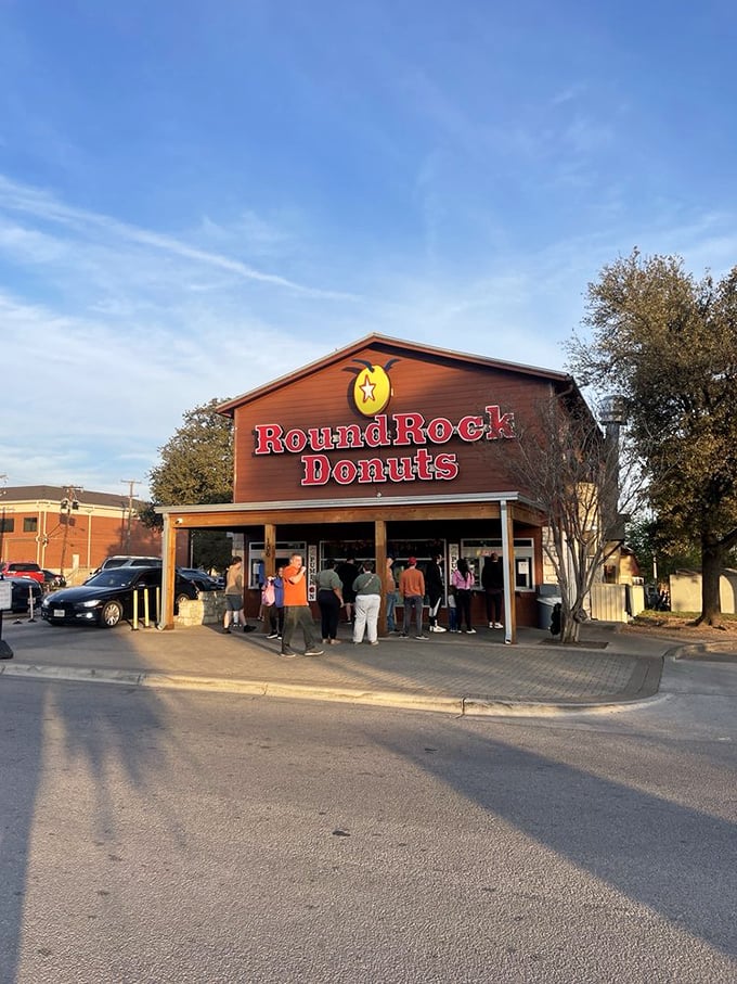 The iconic wooden and limestone facade of Round Rock Donuts stands proudly under Texas skies, beckoning donut pilgrims with its famous red signage.