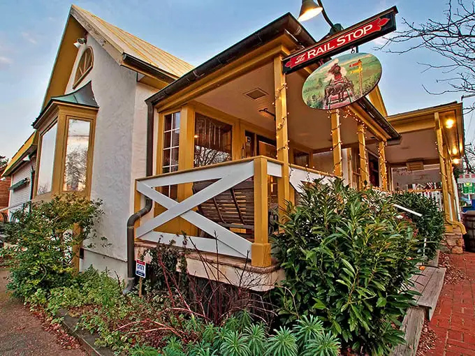 The charming yellow exterior of The Rail Stop beckons like an old friend, promising comfort and culinary delights beneath that distinctive red sign.