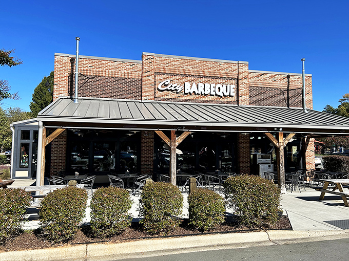 The brick fortress of flavor stands proud with its metal roof and welcoming red umbrellas—a barbecue beacon calling hungry travelers home.