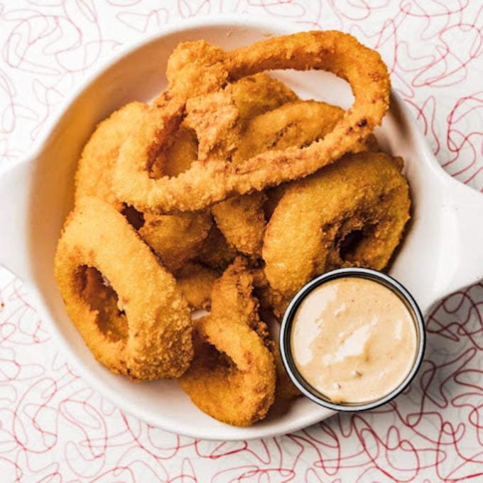 Onion rings wearing their crunchy coats with pride, ready to take a dip in that creamy sauce—a circular celebration of texture and taste.