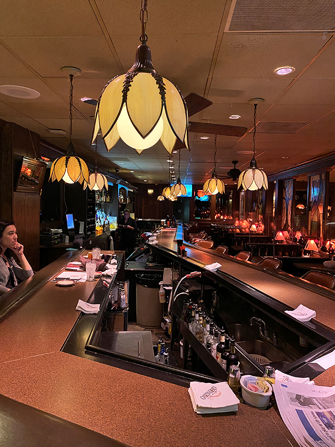The bar area glows with possibility – each pendant light illuminating decades of celebrations, deals, and first dates.