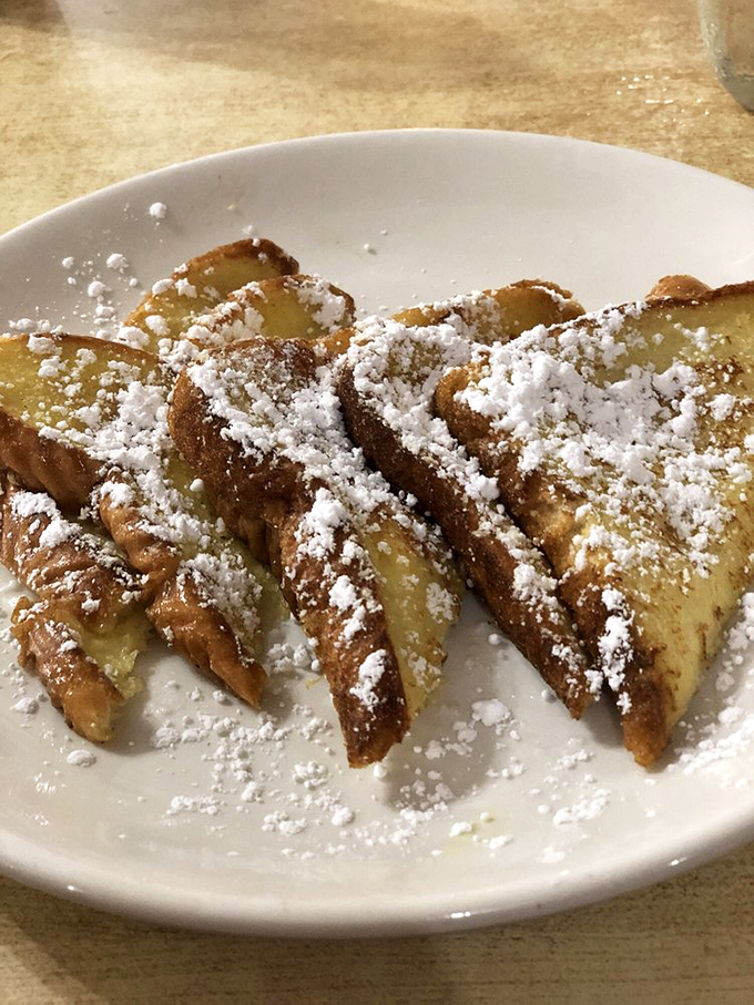 French toast transformed into dessert for breakfast—powdered sugar snowdrifts on golden bread islands. Your pancreas is already writing its resignation letter.