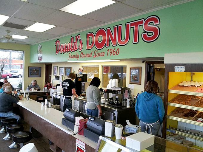 The dance of donut commerce—staff moving with practiced efficiency while customers contemplate life's sweetest decisions at the counter.