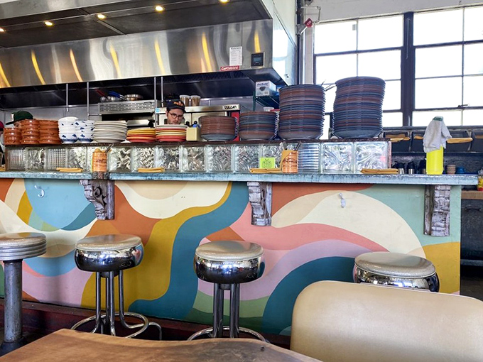 Behind the colorful counter, culinary magic happens. The whimsical waves painted below remind you this isn't your grandfather's greasy spoon—unless your grandfather was incredibly hip.