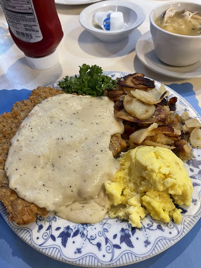 Country cooking at its finest—gravy cascading over chicken fried steak like a savory waterfall, with eggs and potatoes standing by for backup.