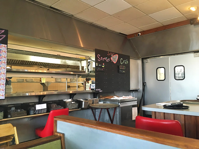 Behind the scenes where short-order symphonies are composed. That "Service with Care" sign isn't just decoration—it's the kitchen constitution.