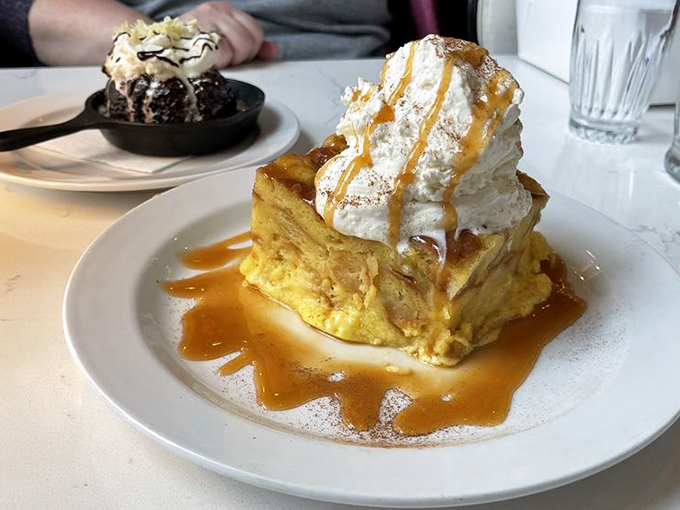 Bread pudding that defies gravity and restraint – topped with a cloud of whipped cream and drizzled with caramel that demands to be photographed, then devoured.
