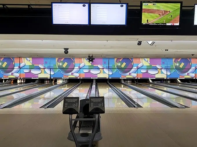 Polished lanes stretch toward colorful backdrops, where digital screens keep score while a baseball game plays nearby—multitasking at its finest.