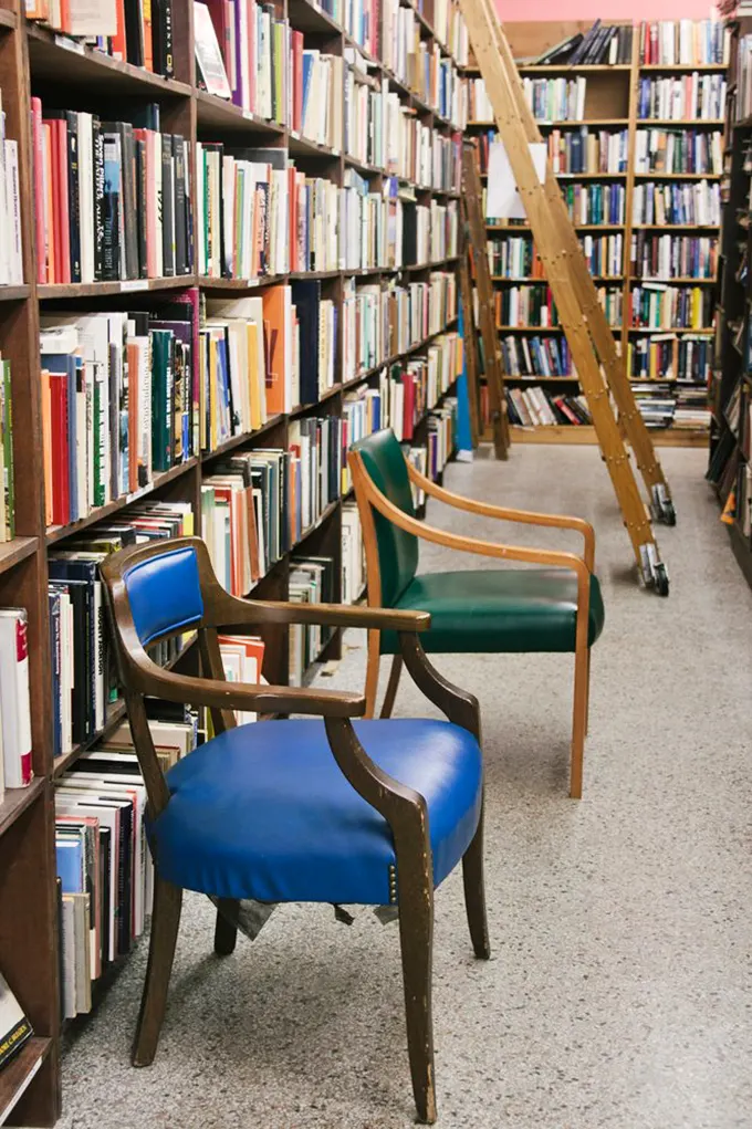 Literary canyons formed by towering shelves, with comfortable chairs inviting you to sit and sample. The wooden ladder isn't decorative—it's an essential exploration tool.